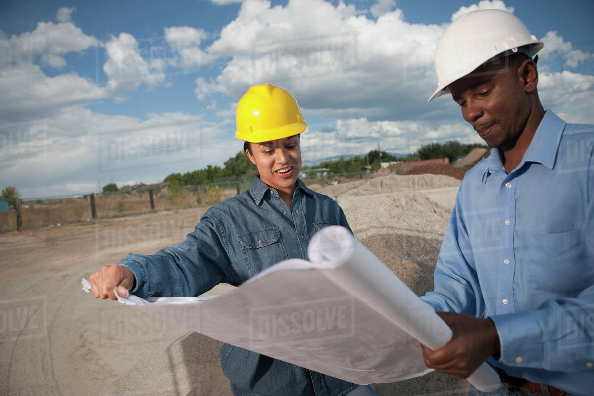 Two construction workers discussing blueprints on building site ...