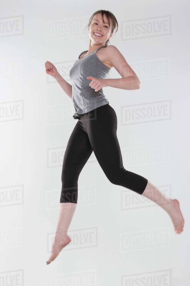 Portrait of young woman jumping, studio shot - Stock Photo - Dissolve