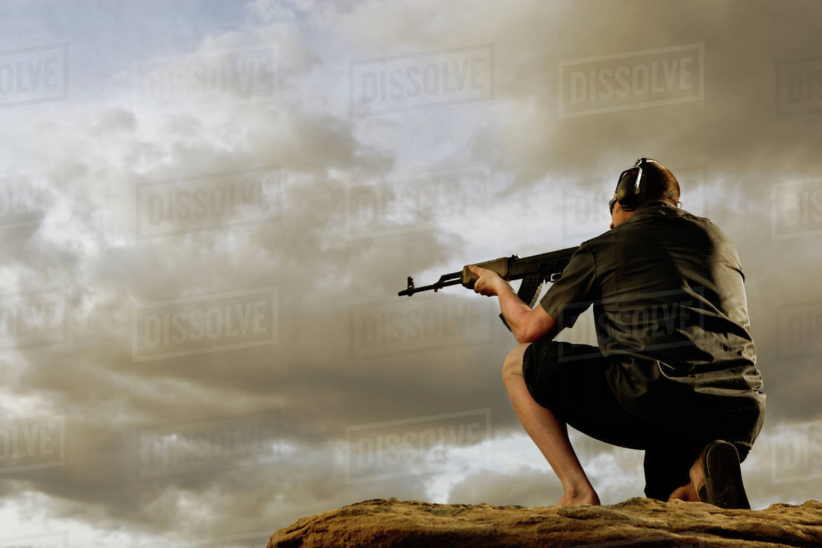 Man aiming gun on rocks - Royalty-free Stock Photo | Dissolve