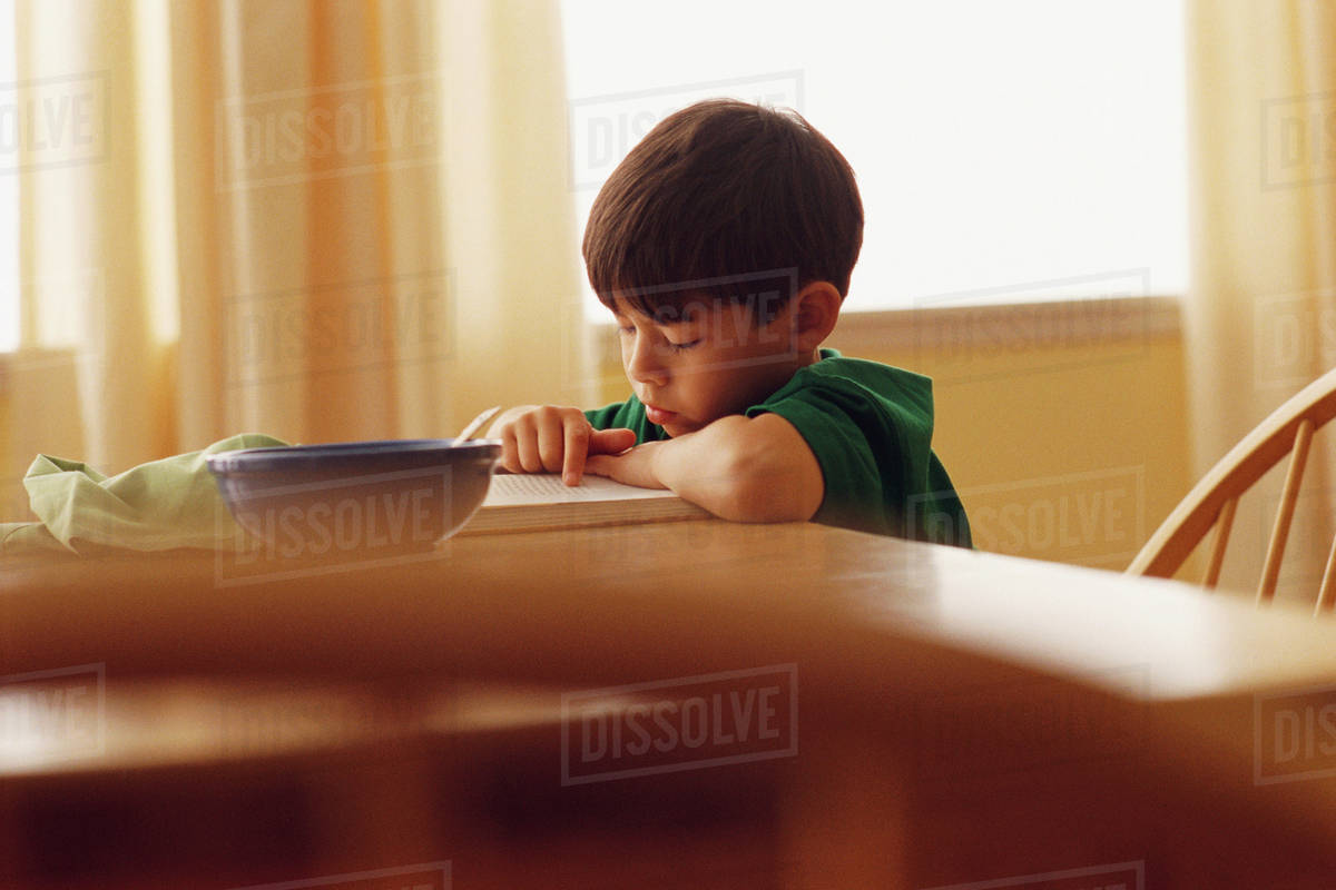 Young boy reading at the kitchen table - Stock Photo - Dissolve