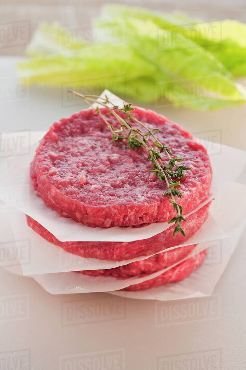 Hamburger patties in stack with salad leaves in background - Stock ...