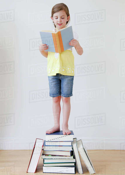 Child reading while standing on books - Royalty-free Stock Photo | Dissolve