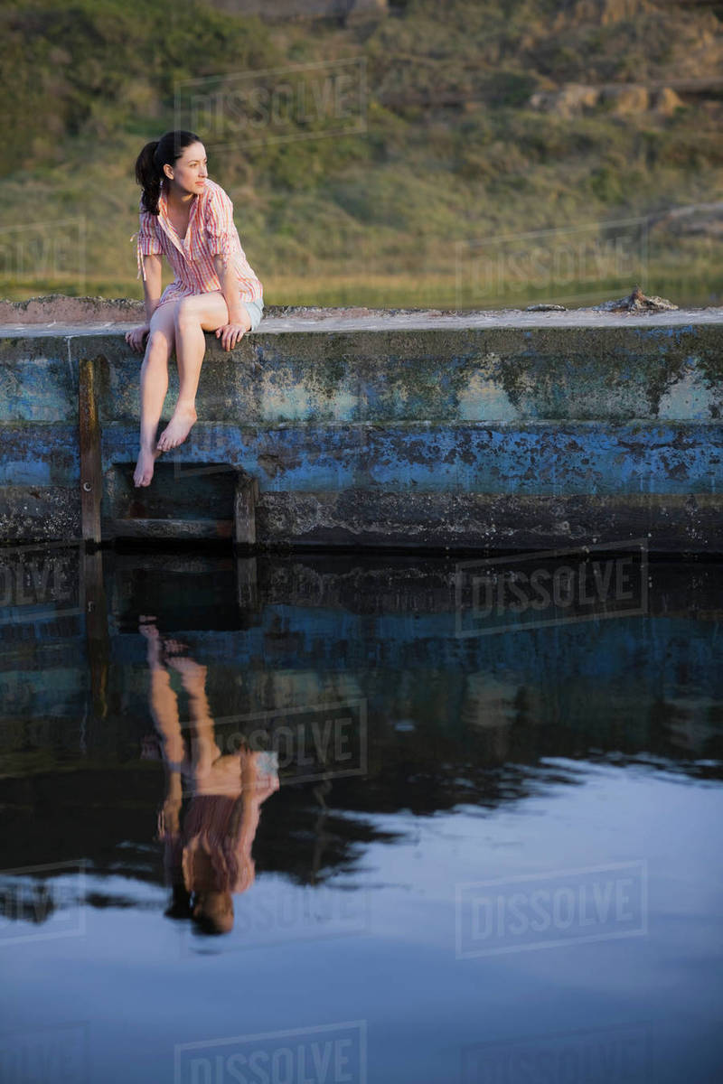 A woman sitting on a stone wall by water - Stock Photo - Dissolve