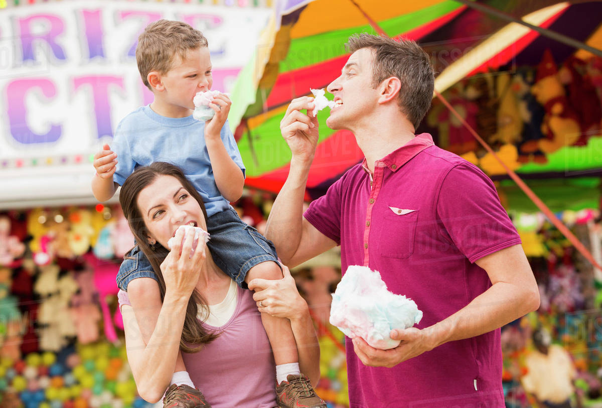 Happy family with son (4-5) in amusement park eating cotton candy ...