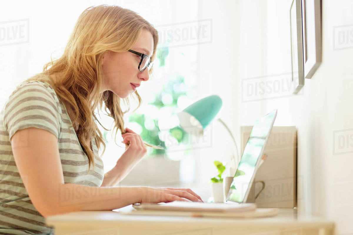Side-view of young woman working on laptop at home - Royalty-free Stock ...
