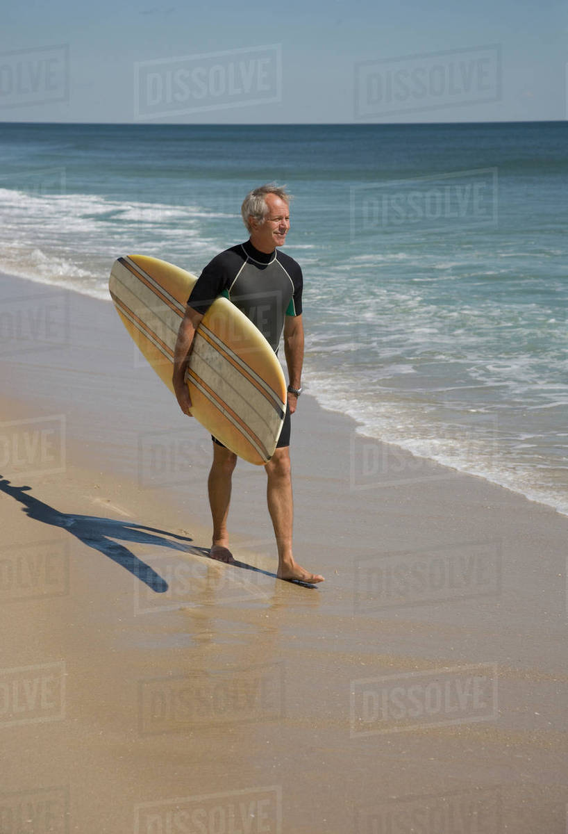 Man carrying surfboard at beach - Stock Photo - Dissolve