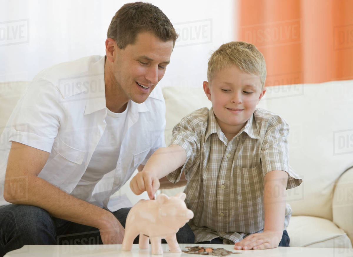 Father and son putting money in piggy bank - Stock Photo - Dissolve