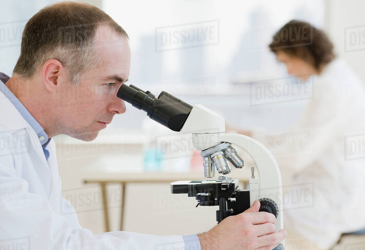 Male scientist looking into microscope - Stock Photo - Dissolve