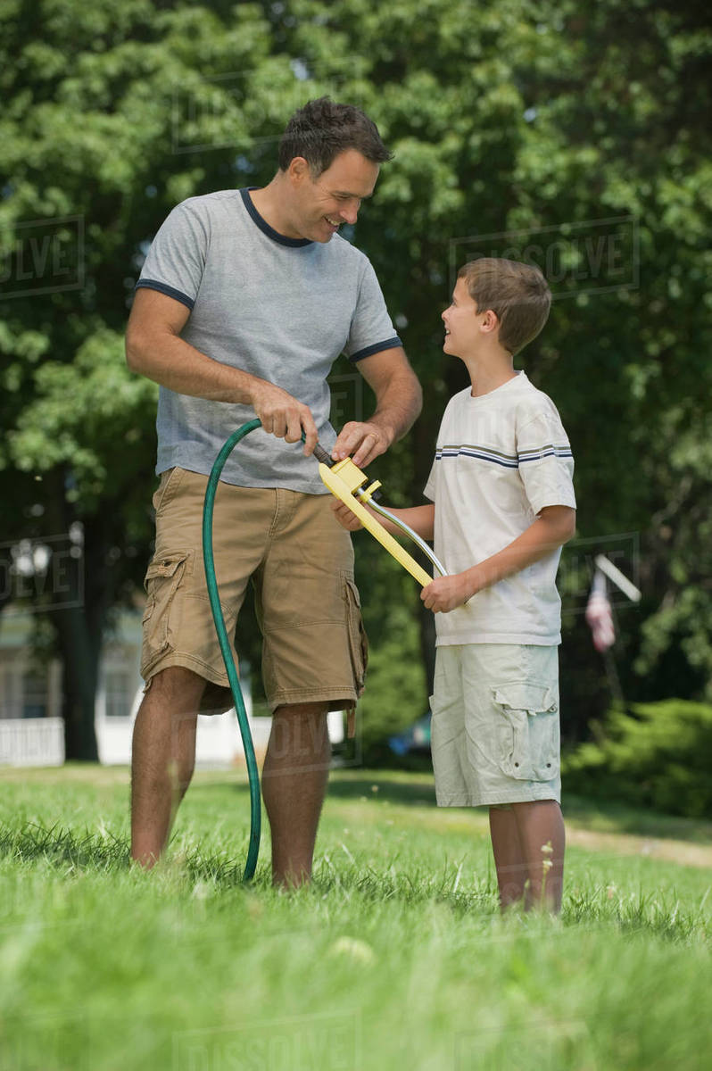 Boy helping father with sprinkler in backyard - Stock Photo - Dissolve