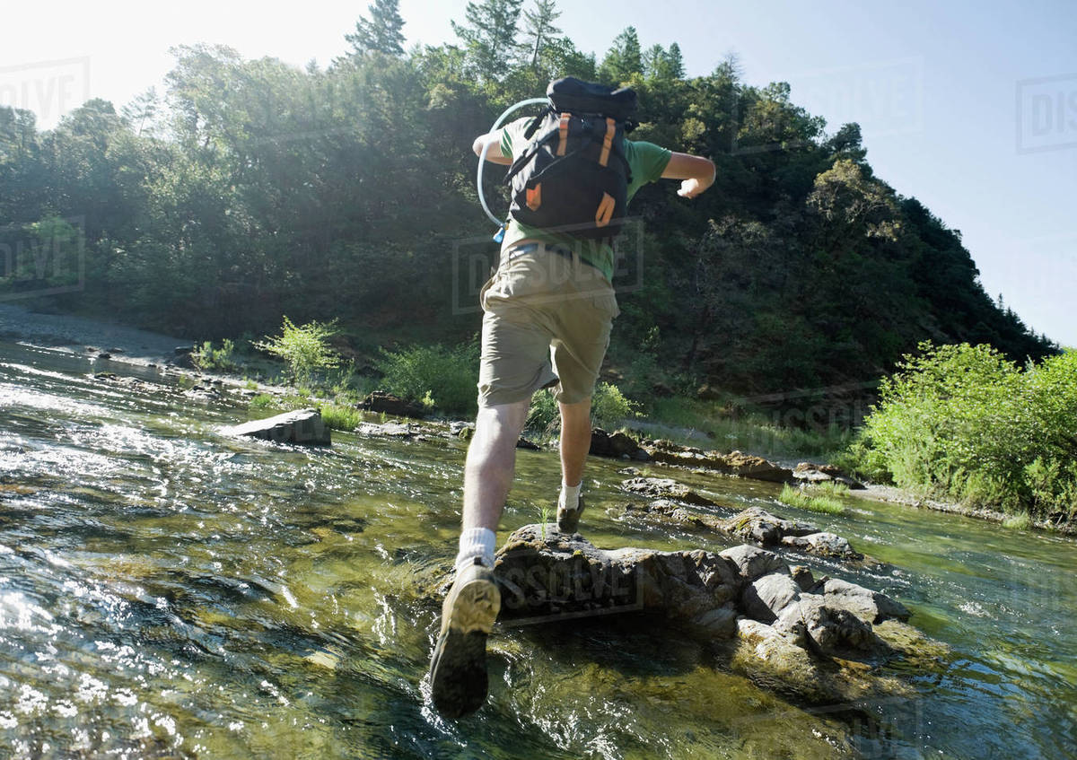 Man jumping across river on rocks - Stock Photo - Dissolve