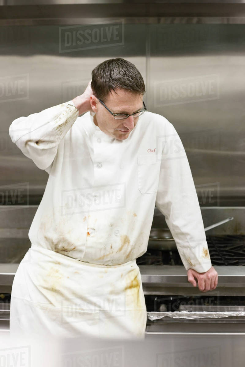 Tired chef leaning against stove - Stock Photo - Dissolve