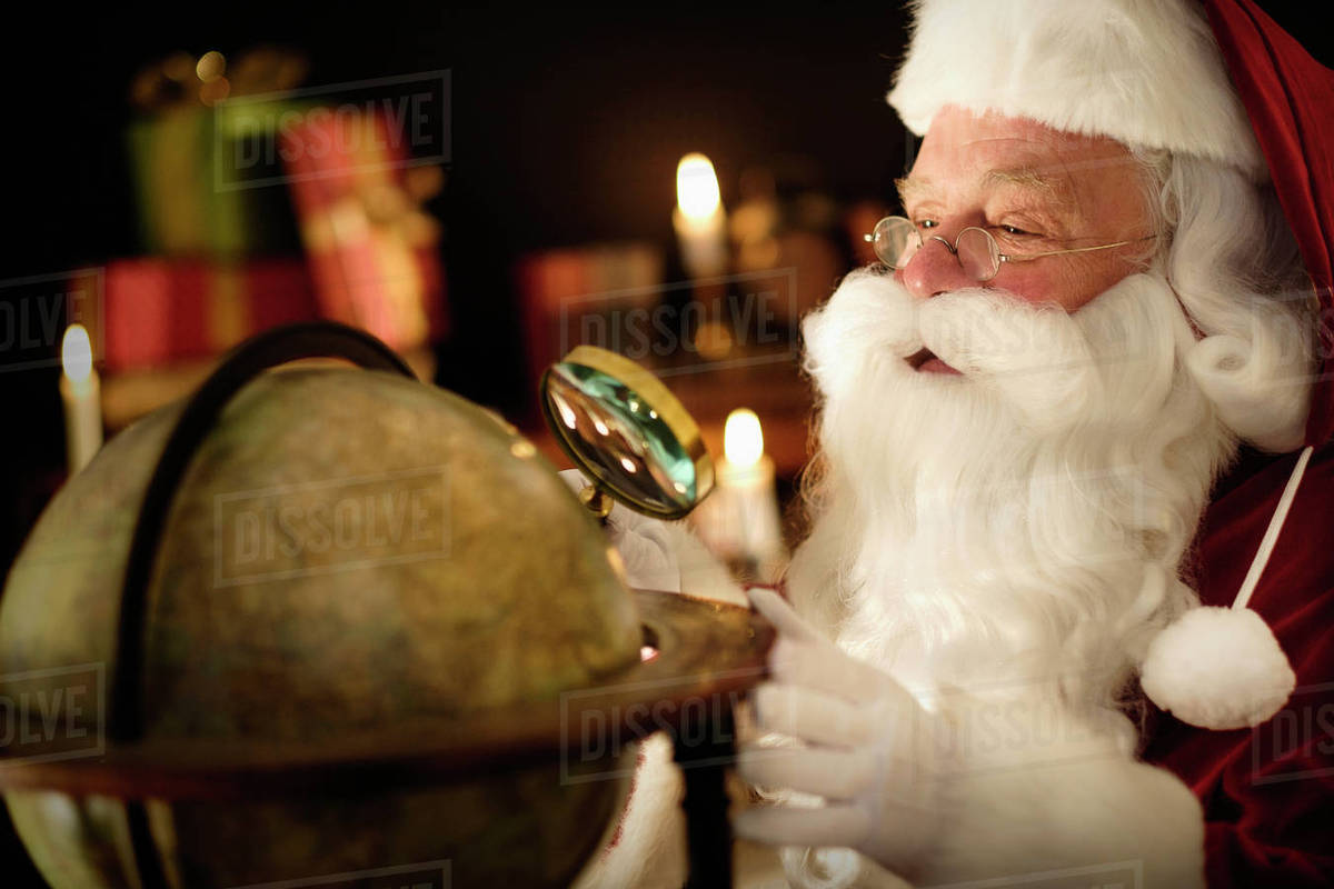 Santa Claus looking through magnifying glass at globe - Royalty-free ...