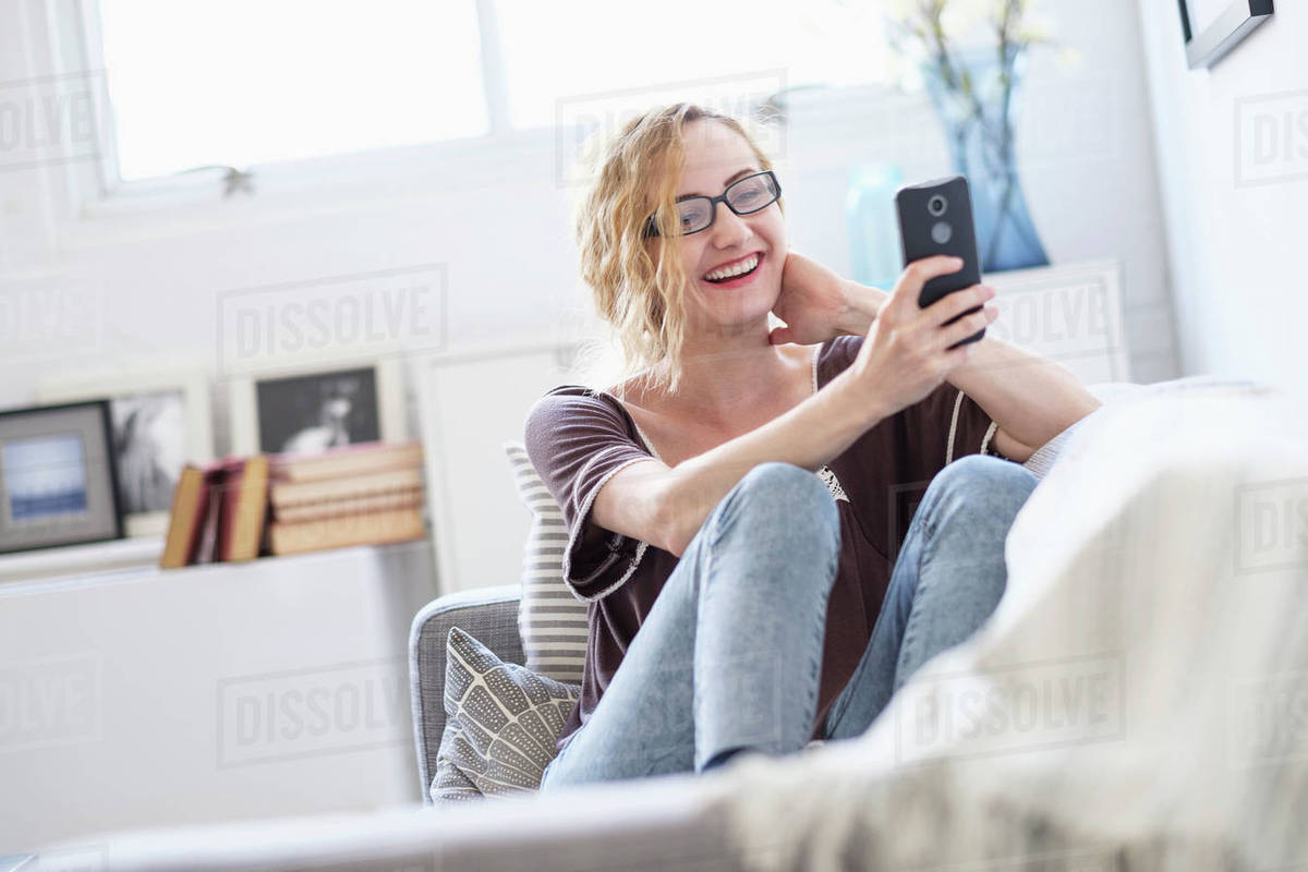 Woman sitting on sofa and using mobile phone - Royalty-free Stock Photo ...