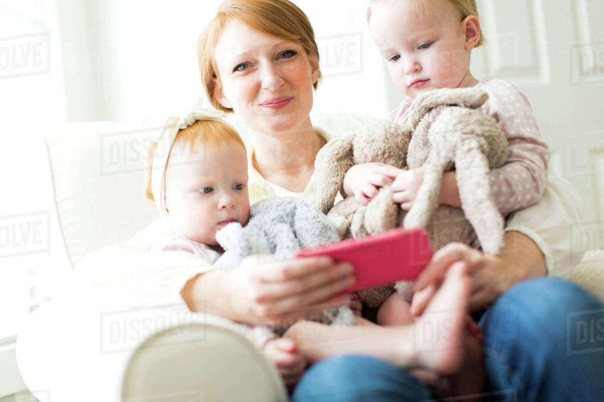 Portrait of mother using smart phone with daughters ( 12-17 months ...