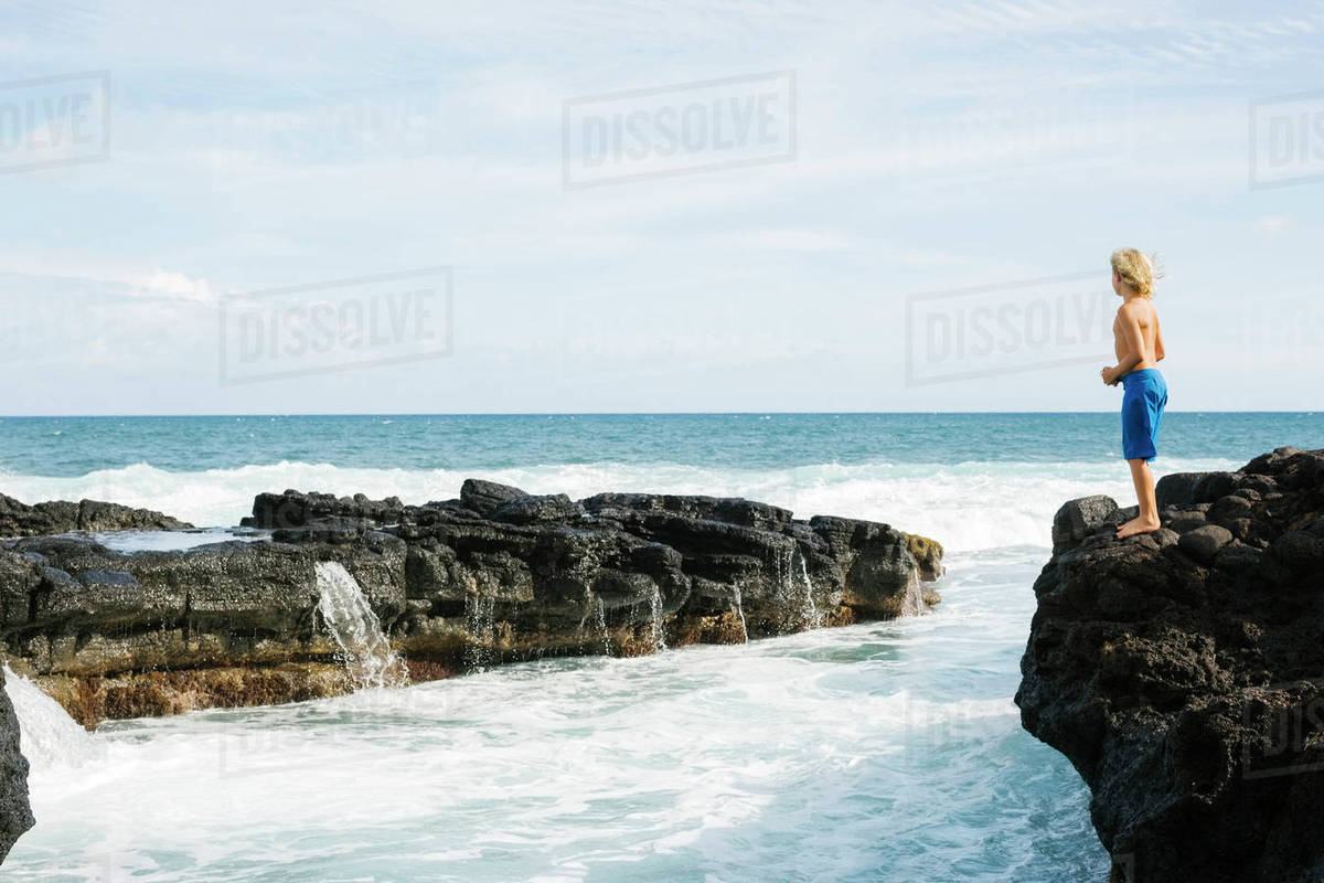 Boy (8-9) standing on rock against blue sky - Royalty-free Stock Photo ...