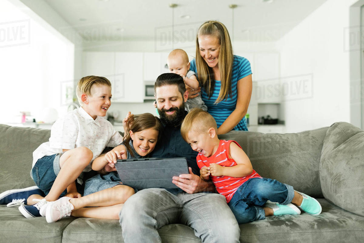 Family with four children (6-11 months, 2-3, 6-7) using digital tablet ...