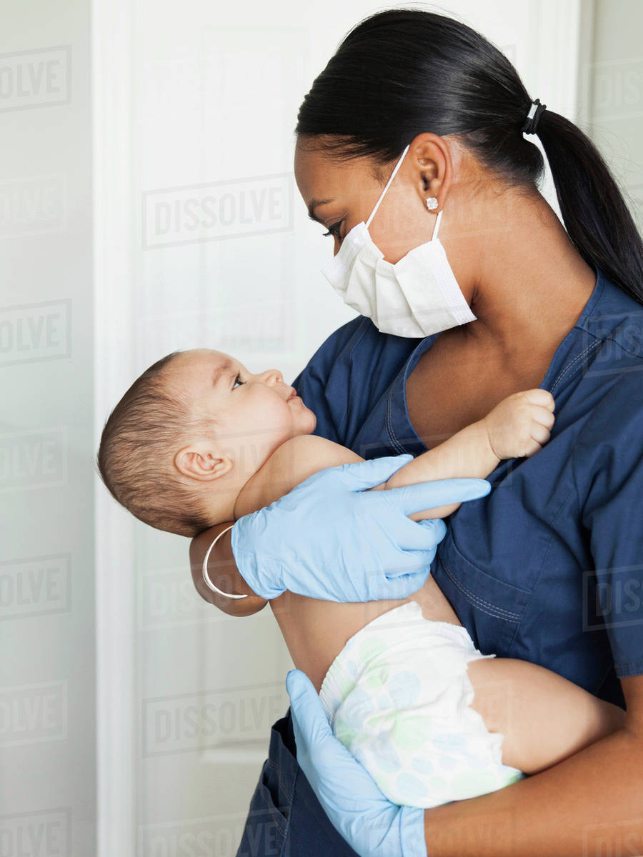 Nurse holding in arms baby boy (2-5 months) - Stock Photo - Dissolve