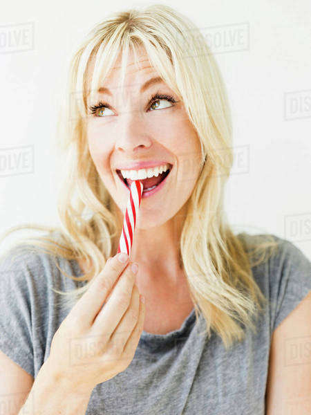 Woman eating candy cane, studio shot - Stock Photo - Dissolve