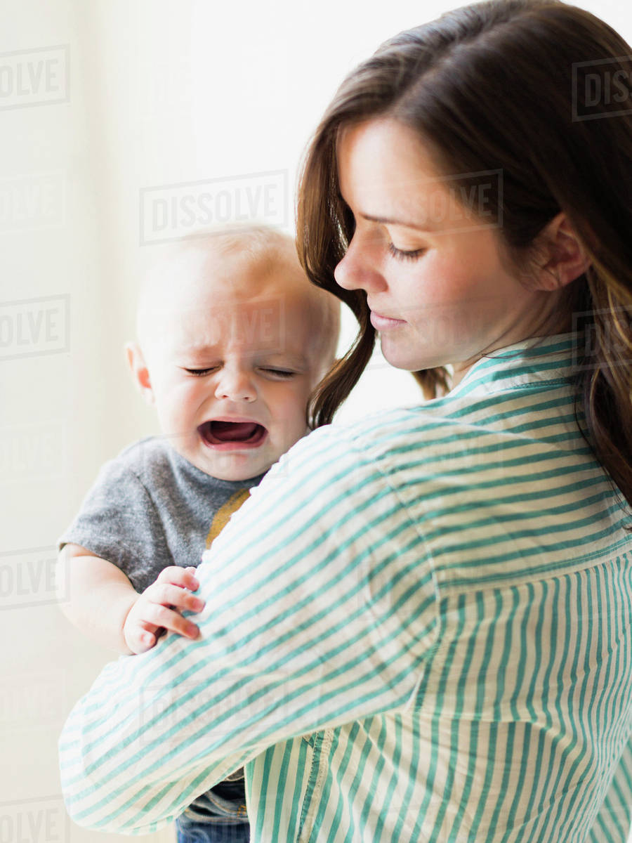 Mother consoling baby boy (6-11 months) indoors - Stock Photo - Dissolve