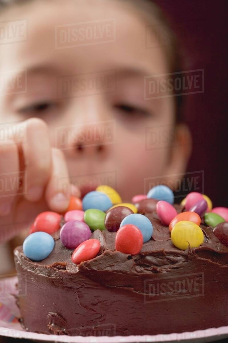 Little girl taking chocolate bean from birthday cake - Stock Photo ...