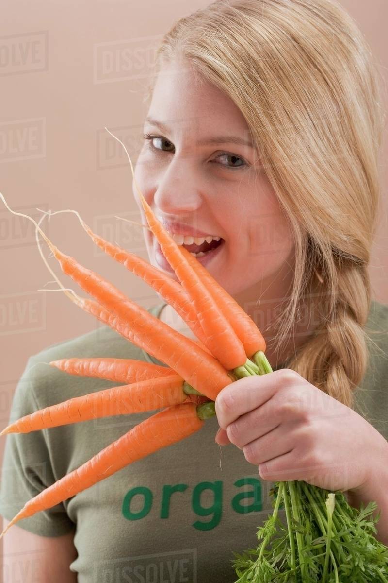 Woman biting a fresh carrot - Stock Photo - Dissolve