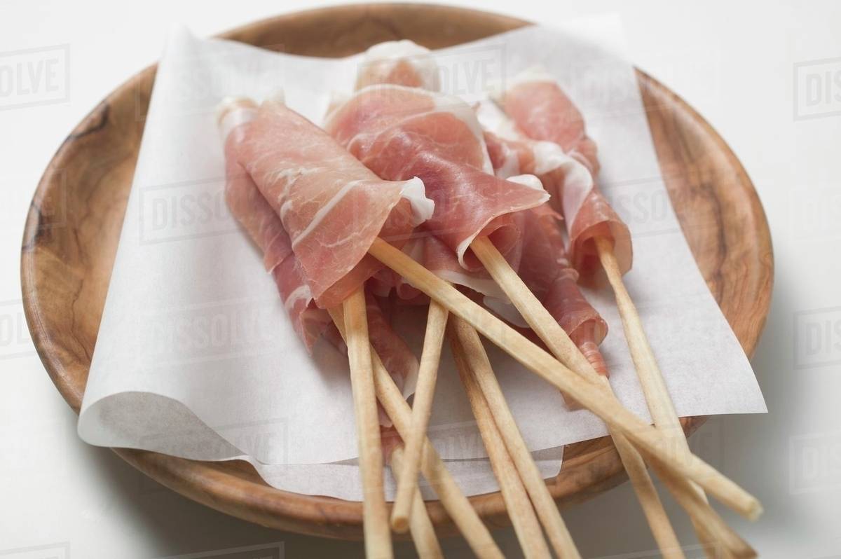Grissini wrapped in raw ham on wooden plate - Stock Photo - Dissolve