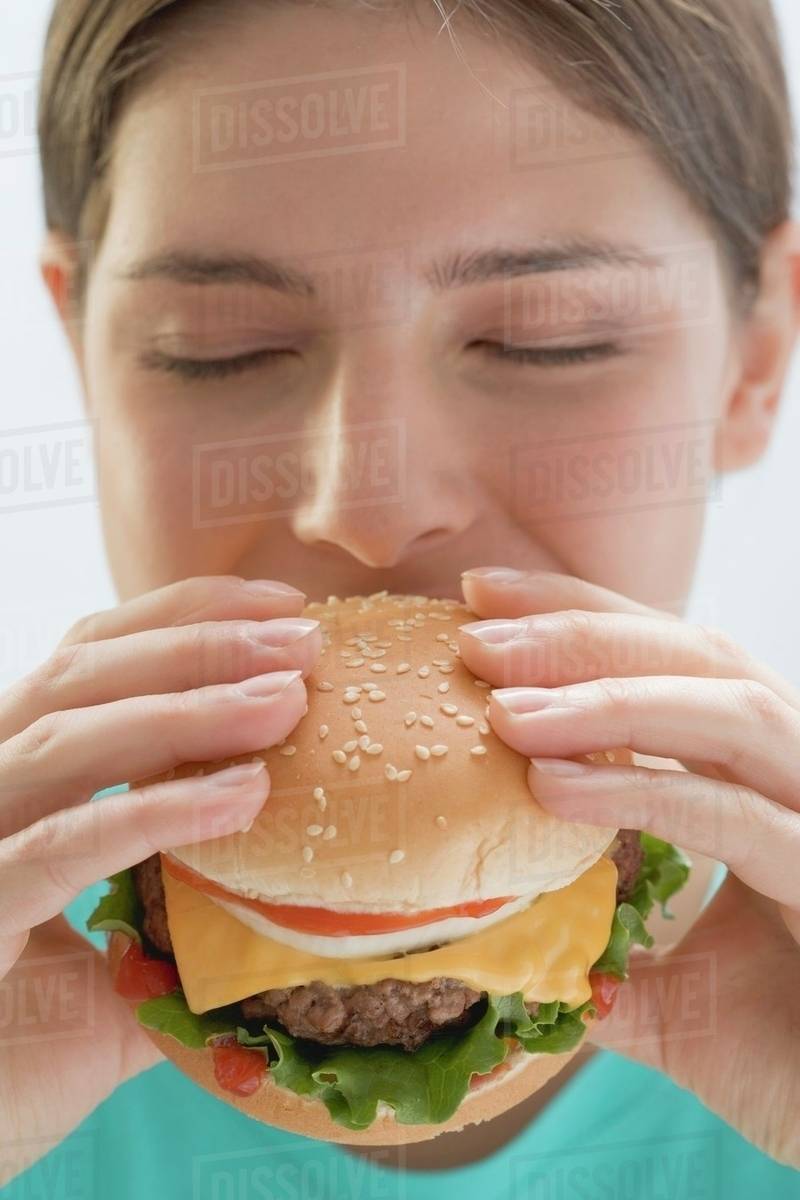 Young woman biting into cheeseburger - Stock Photo - Dissolve