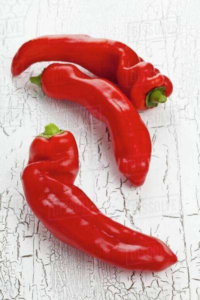 Three red pointed peppers on a white wooden table - Stock Photo - Dissolve