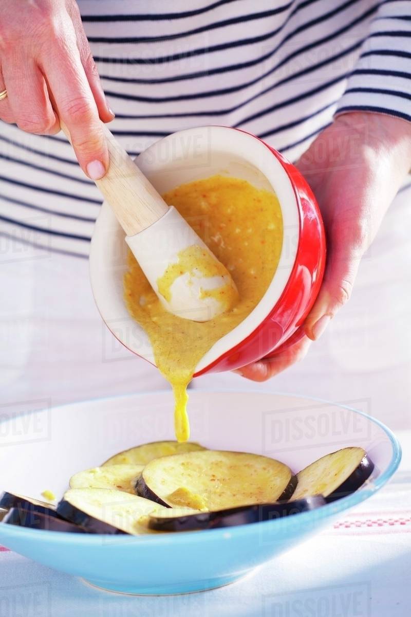 A woman pouring mustard marinade onto sliced aubergine - Royalty-free ...