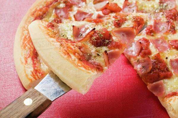 Ham, cheese and tomato pizza with slice on server - Stock Photo - Dissolve