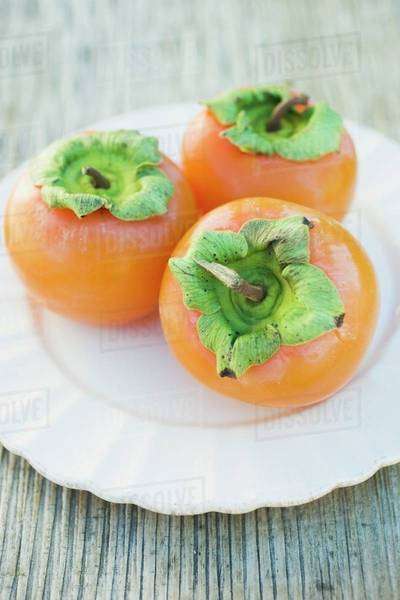 Three Sharon fruits on white plate - Royalty-free Stock Photo | Dissolve