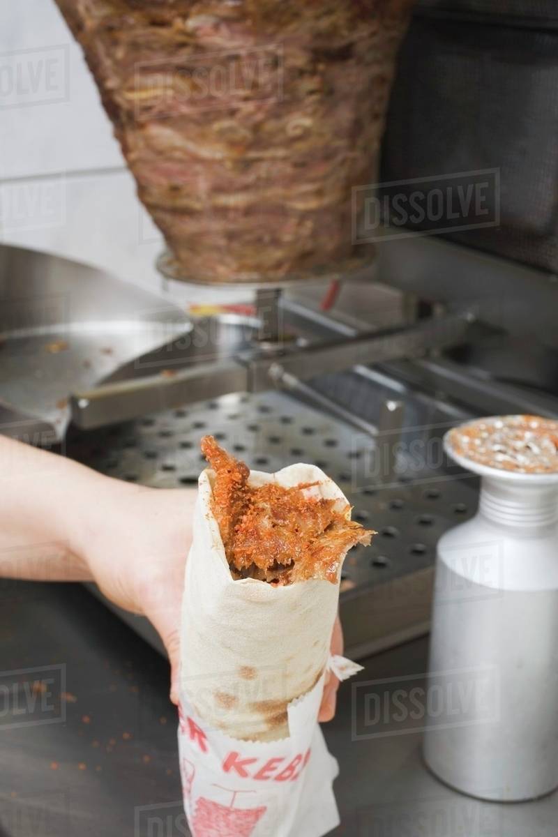 Hand holding doner wrap in a snack bar - Stock Photo - Dissolve