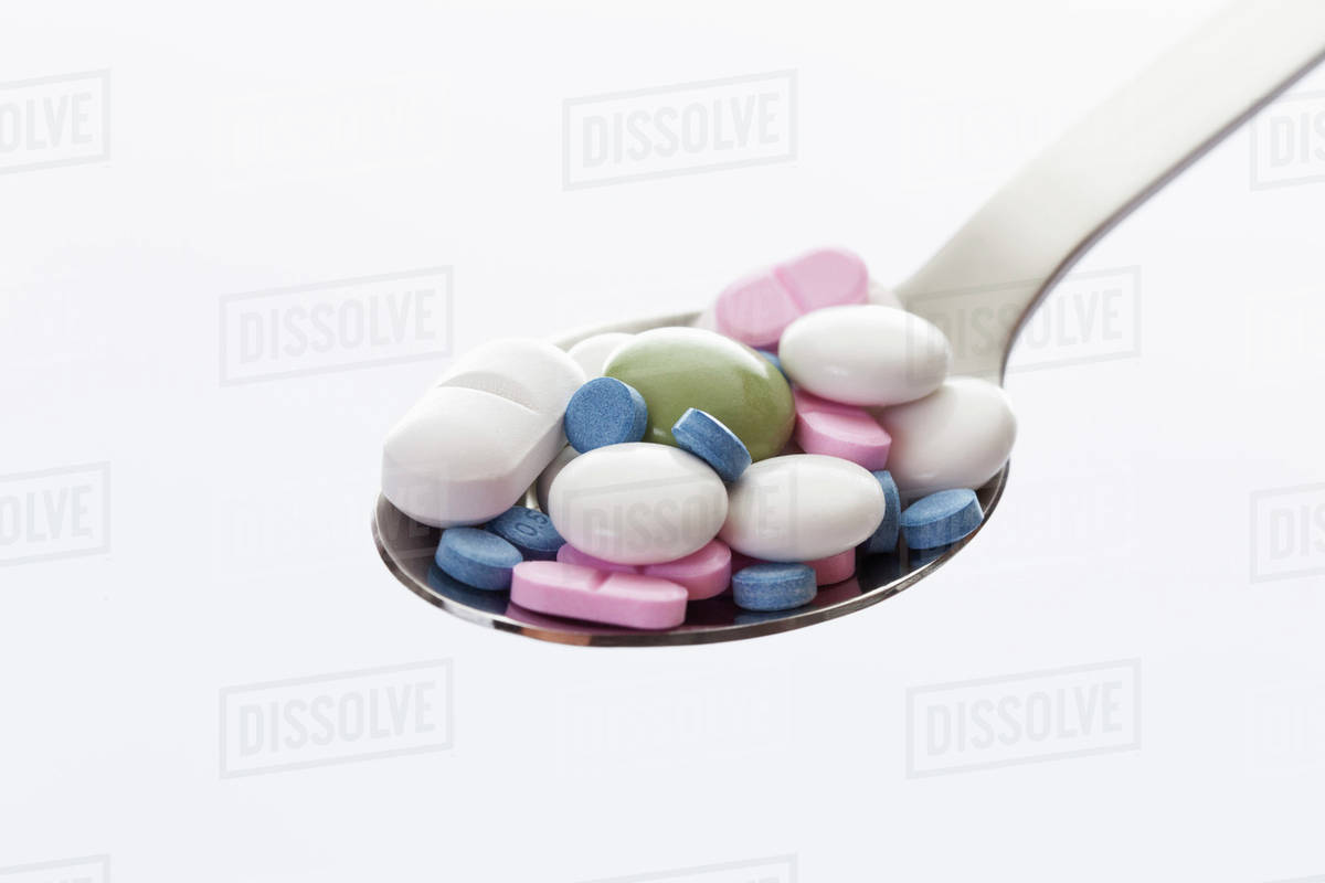 Mixed tablets in spoon against white background - Stock Photo - Dissolve