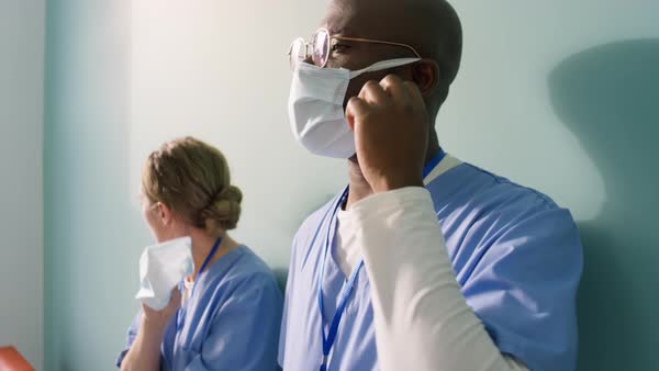 Exhausted nurses leaning on wall in hospital removing surgical masks ...