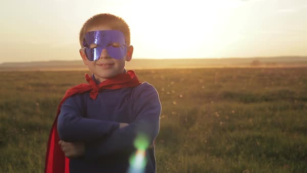 Boy dressed with a Superman cape running in a field, looking into the ...
