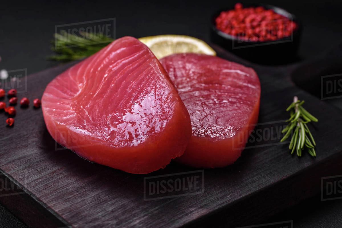 Two fresh slices of raw tuna fillet with spices and herbs on a dark ...