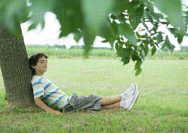 Boy sitting on ground, leaning against tree, eyes closed - Royalty-free ...