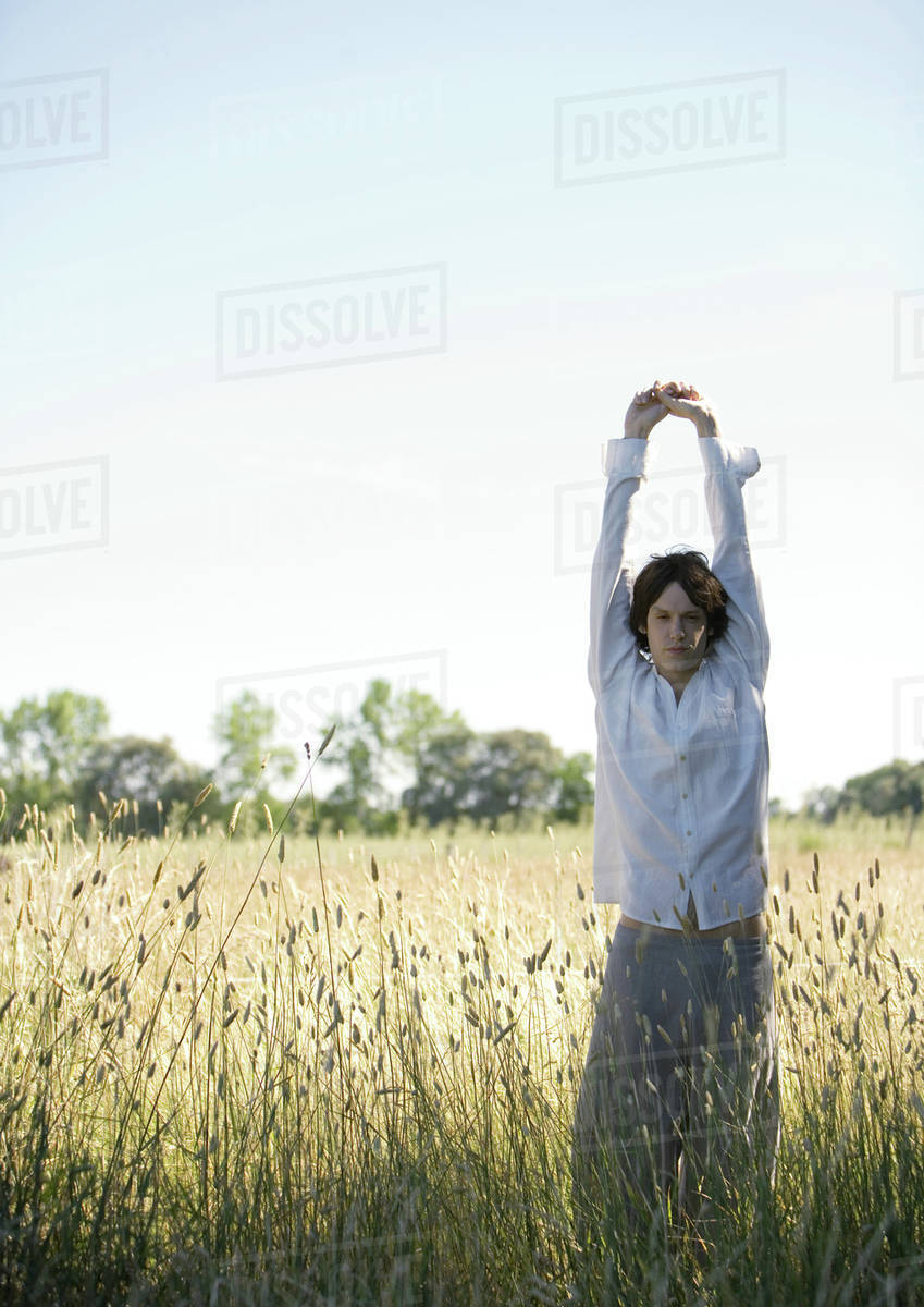 Man standing stretching arms over head in field - Stock Photo - Dissolve