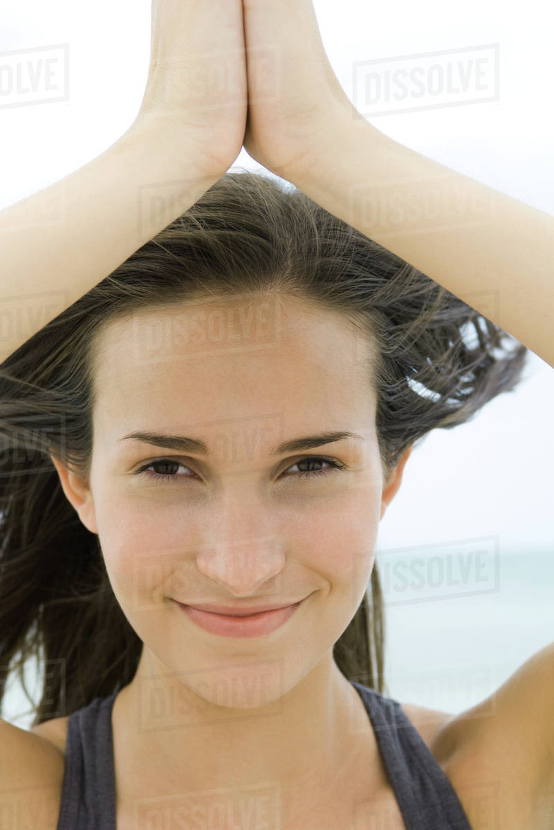 Young woman with hands raised over head in prayer position, smiling at ...