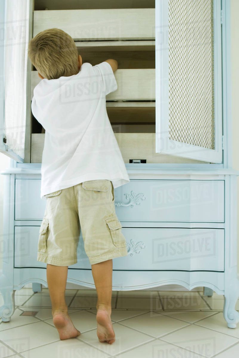 Boy reaching inside armoire, rear view - Stock Photo - Dissolve