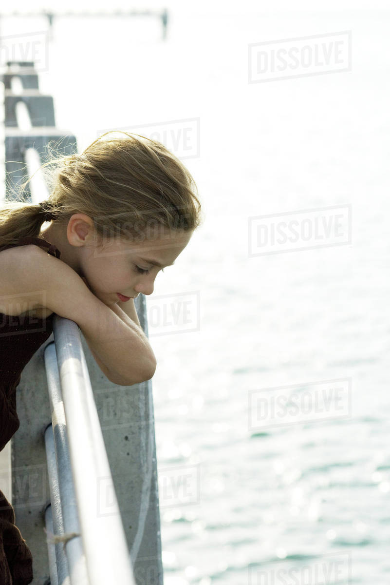 Girl leaning over railing on pier, looking down at water, side view ...