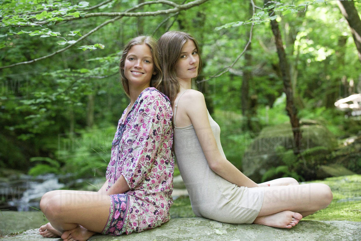 Female friends sitting back to back on rock, portrait - Stock Photo ...