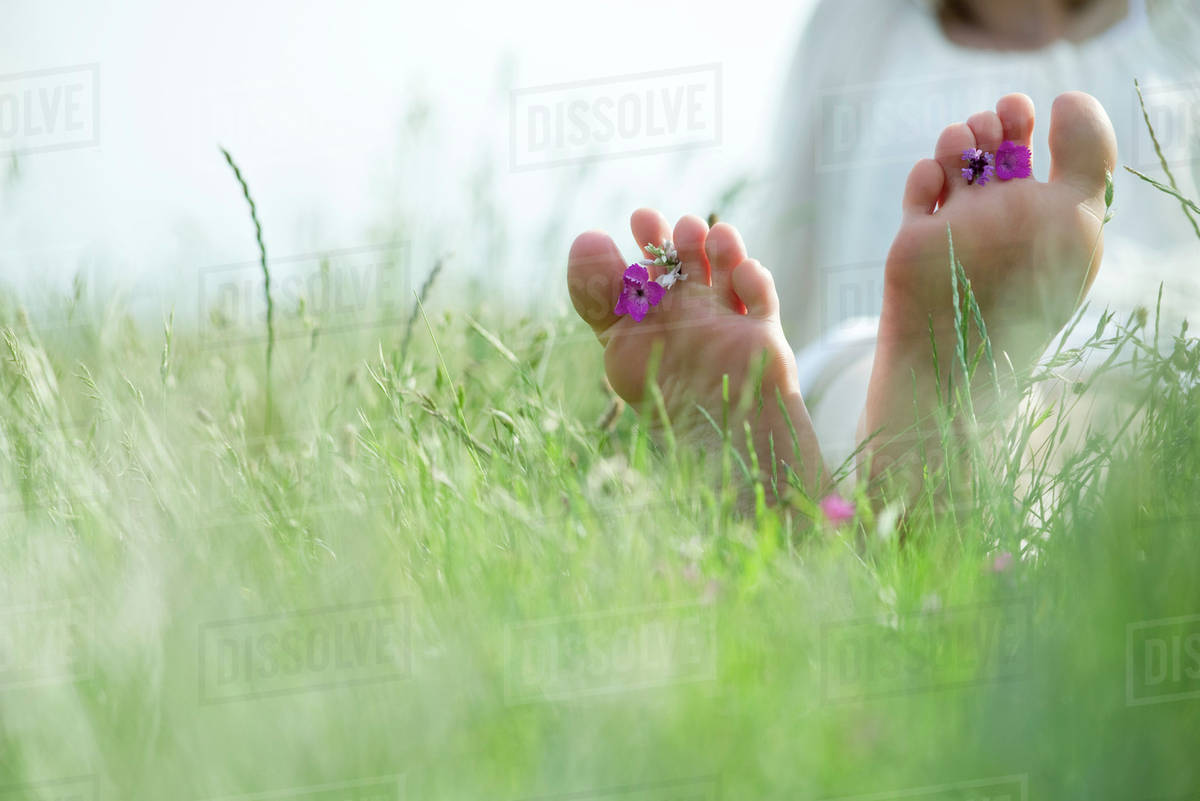 Barefoot young woman sitting in grass with wildflowers between toes ...