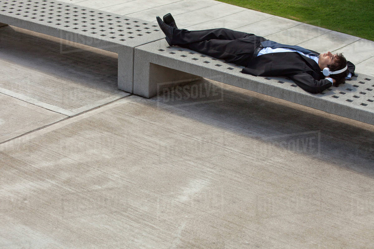 Young businessman napping on park bench with headphones on - Stock ...