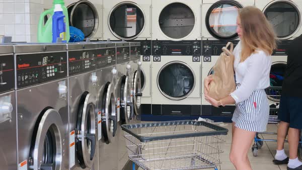 Young woman comes to public laundry to wash clothes from bag - Stock ...