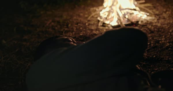 Soldier sleeping on the ground near a blazing campfire at night in a ...