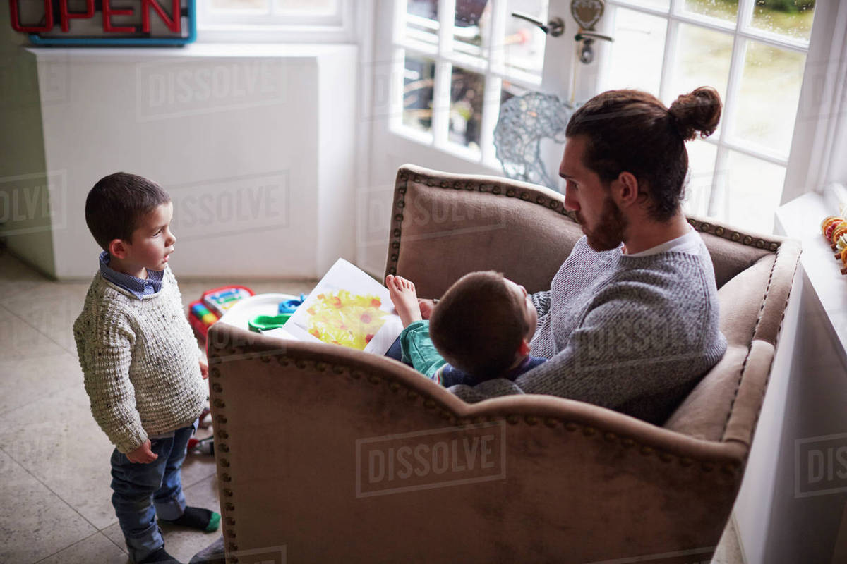 Father sitting in chair at home reading story to sons - Royalty-free ...