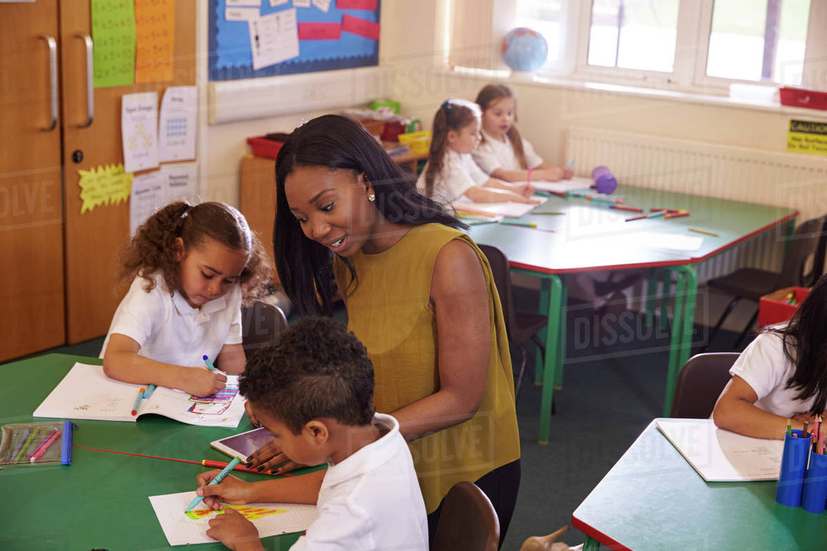 Female elementary school teacher helping pupils at desk - Royalty-free ...