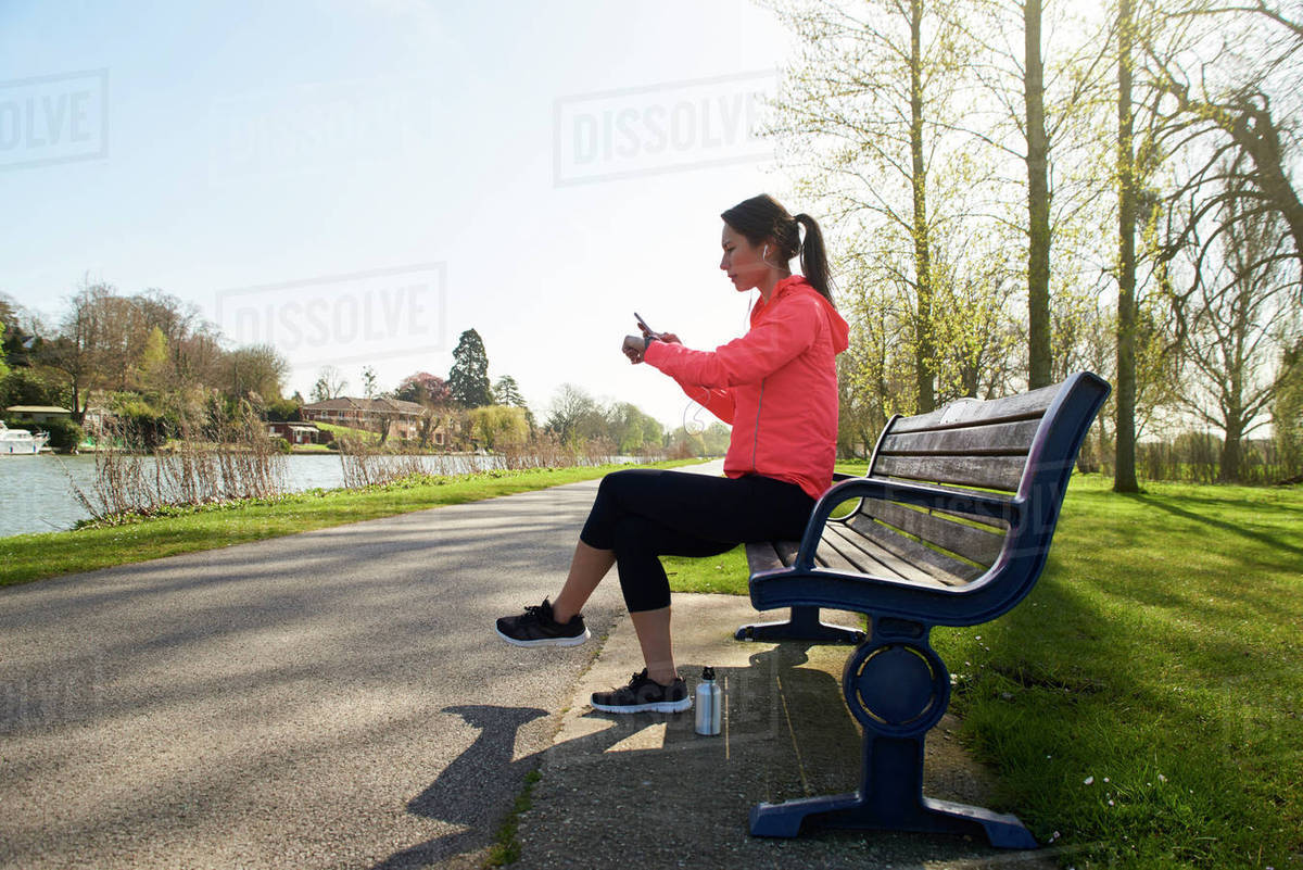 Young Woman Sitting On Park Bench Checking Activity Tracker - Royalty ...