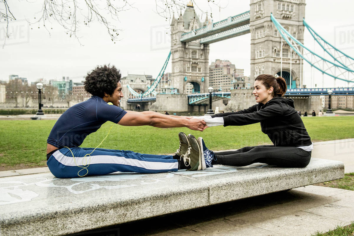 A young couple limbering up together for a jog near to Tower Bridge in ...